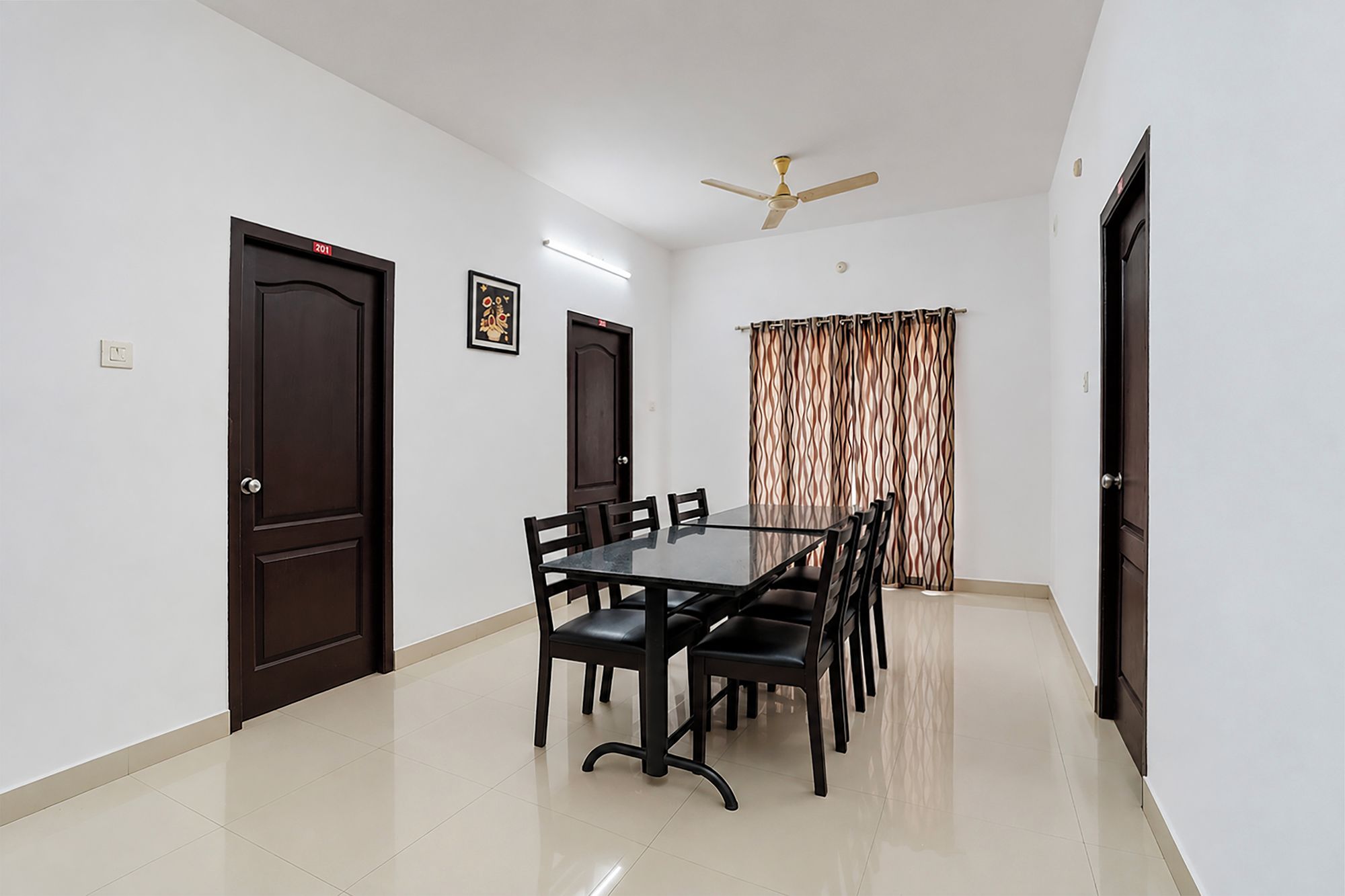 Quarto com mesa de jantar, cadeiras, ventilador de teto e cortina estampada.