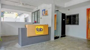Bancada de recepção com placa 'fab hotels', uma janela com grades de metal e uma porta com moldura de madeira.