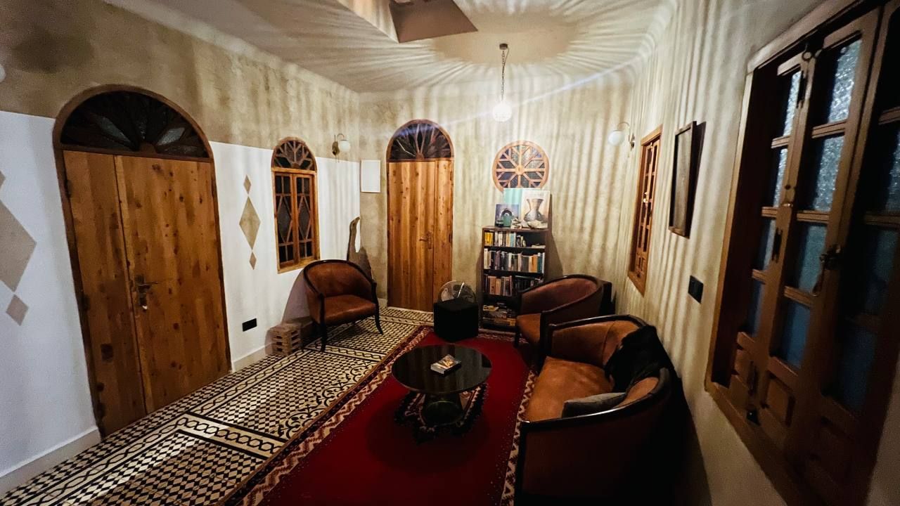 Quarto com carpete estampado, portas de madeira, estante de livros e poltronas de couro.