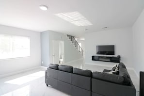 Uma sala de estar moderna com um sofá cinza, uma TV de tela plana e uma escada que leva a outro cômodo.