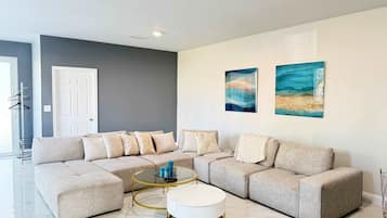 Uma sala de estar moderna com um sofá seccional, uma mesa de centro redonda e duas pinturas penduradas na parede.