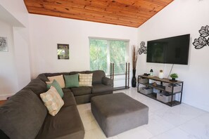 Uma sala de estar moderna com um sofá seccional, uma TV de tela plana e teto de madeira.