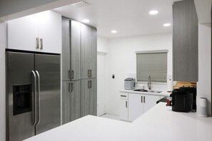 Cozinha moderna com eletrodomésticos de aço inoxidável, armários brancos e uma janela com persianas.