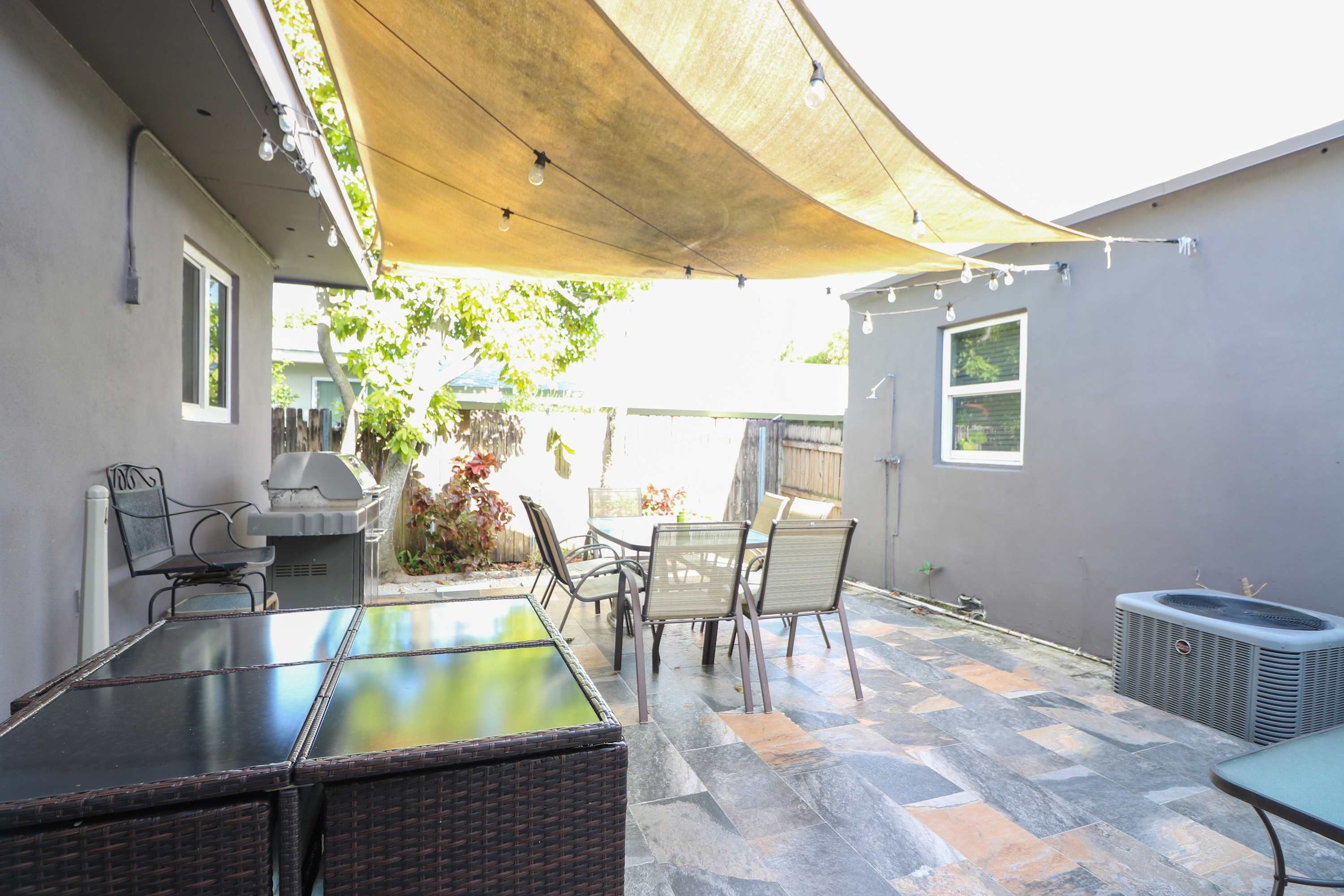 Uma área de pátio externa com mesa e cadeiras, churrasqueira e um espaço de estar coberto.