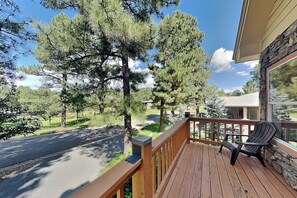 Um deck de madeira com uma cadeira, com vista para uma estrada e árvores.