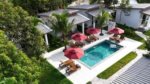 Área de piscina com espreguiçadeiras e guarda-sóis, cercada por vegetação e edifícios modernos.