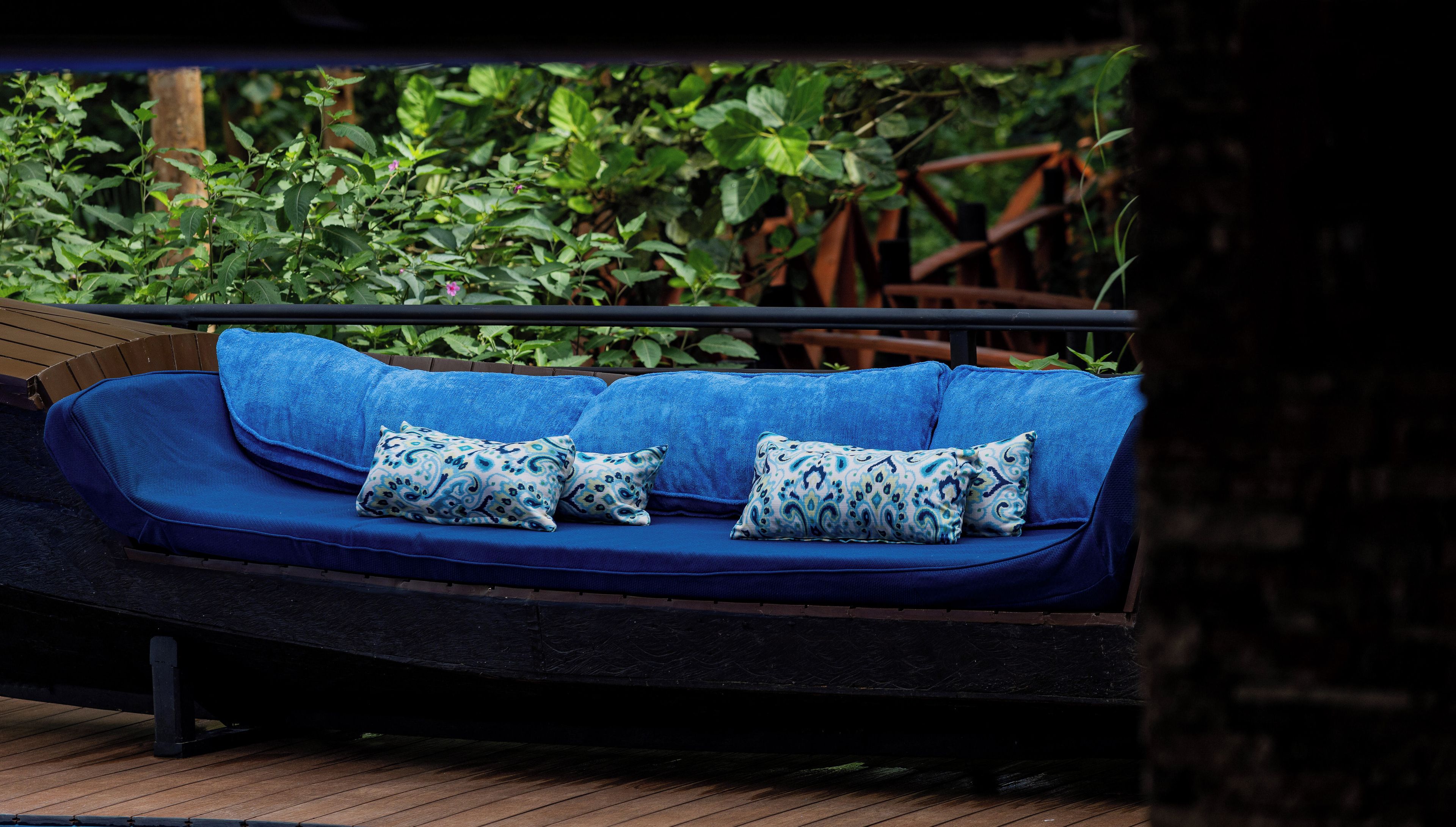 Sofá azul para áreas externas com almofadas estampadas sobre um deck de madeira.