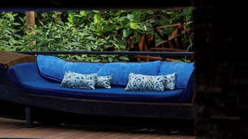 Sofá azul para áreas externas com almofadas estampadas sobre um deck de madeira.
