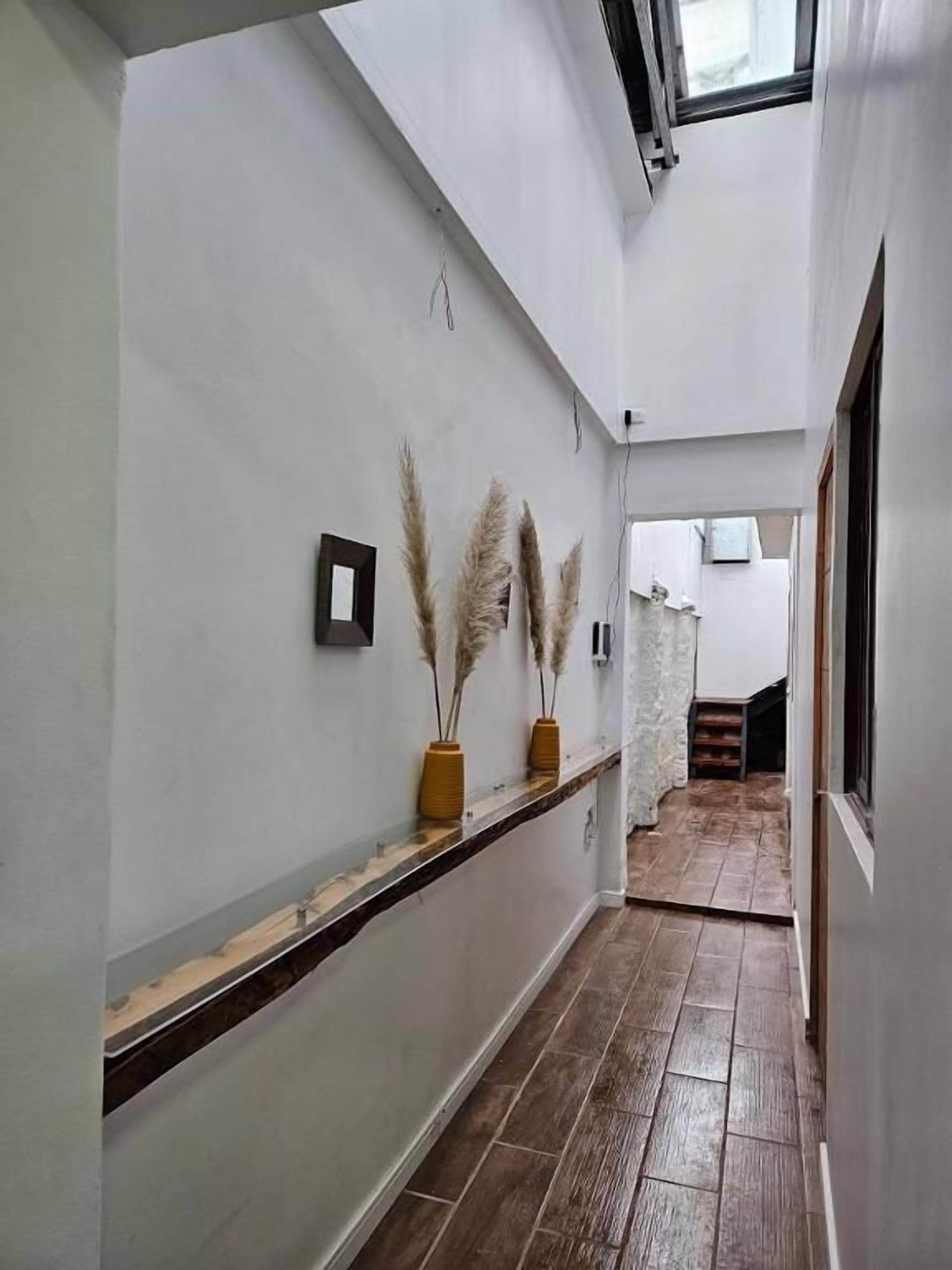 Um corredor com piso de madeira, parede branca e uma janela no final.