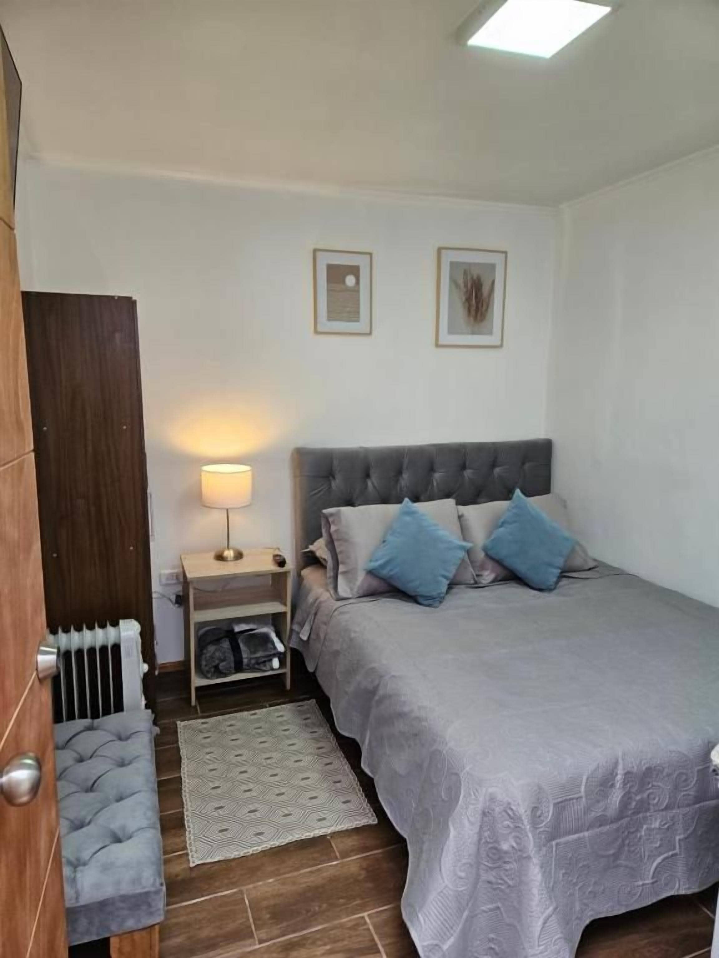 Quarto com cama, mesa de cabeceira, abajur e radiador.
