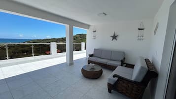 Varanda com sofá branco, cadeiras de vime e mesa de centro redonda.