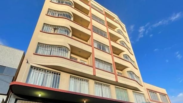 Um hotel com vários andares, fachada plana, janelas amplas e toldo vermelho.