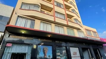 Um hotel com vários andares, fachada plana, janelas amplas e toldo vermelho.