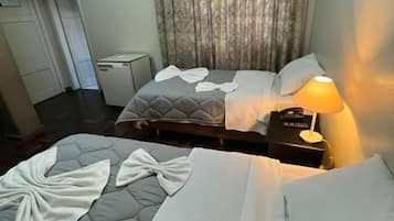 Quarto de hotel com duas camas, uma mesa de cabeceira com abajur e uma pequena escrivaninha com computador.