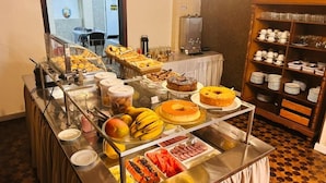 Buffet com diversos alimentos, máquina de café e suporte para copos.