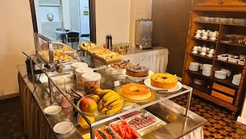 Buffet com diversos alimentos, máquina de café e suporte para copos.