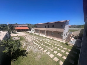 Um pátio com área pavimentada, um edifício com telhado de cerâmica e uma escadaria que leva a um andar superior.