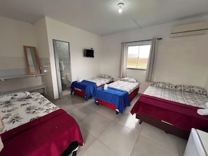 Quarto com quatro camas, espelho, televisão e janela com cortinas.