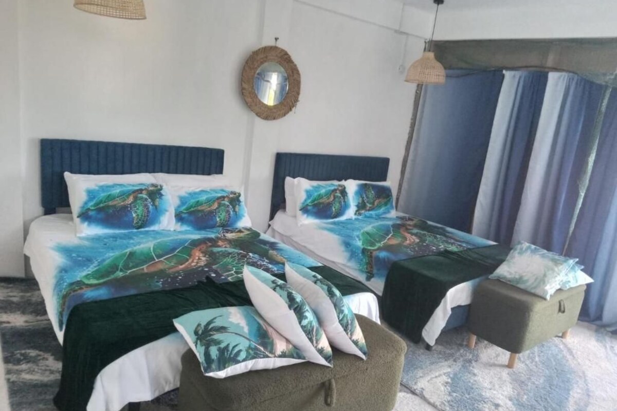 Quarto com duas camas, uma mesa pequena, um espelho e uma cortina.