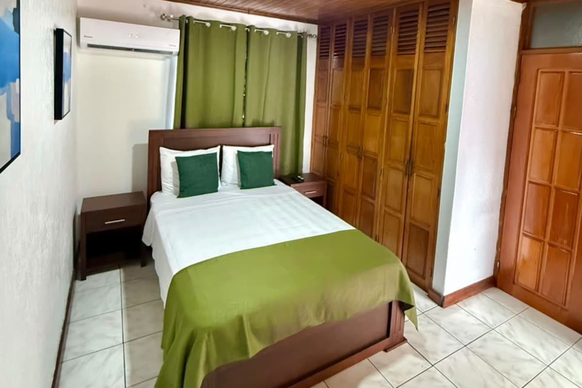Quarto com teto de madeira, cama com roupa de cama verde, guarda-roupa e mesa de cabeceira.