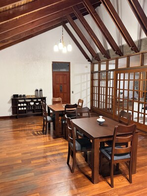 Uma área de refeições com mesa e cadeiras de madeira, cozinha com armários e eletrodomésticos, e uma janela grande com vista.