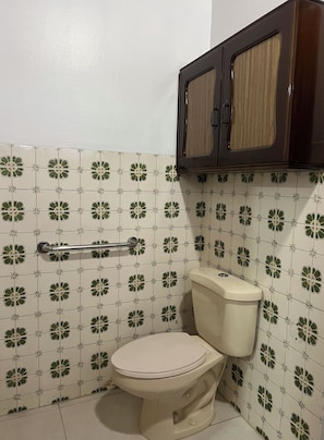 Casa de banho com sanita, barra de apoio e armário.