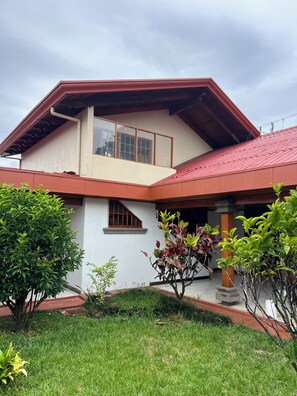 Uma casa de dois andares com telhado vermelho, uma janela grande no andar superior e uma pequena varanda.