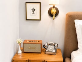 Uma mesa de cabeceira de madeira com um rádio antigo, um telefone e um quadro na parede acima.