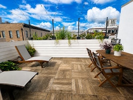Um terraço no telhado com piso de madeira, uma mesa de jantar com cadeiras e plantas em vasos.
