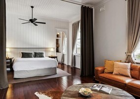 Quarto de hotel com cama, sofá de couro, mesa de centro e ventilador de teto.