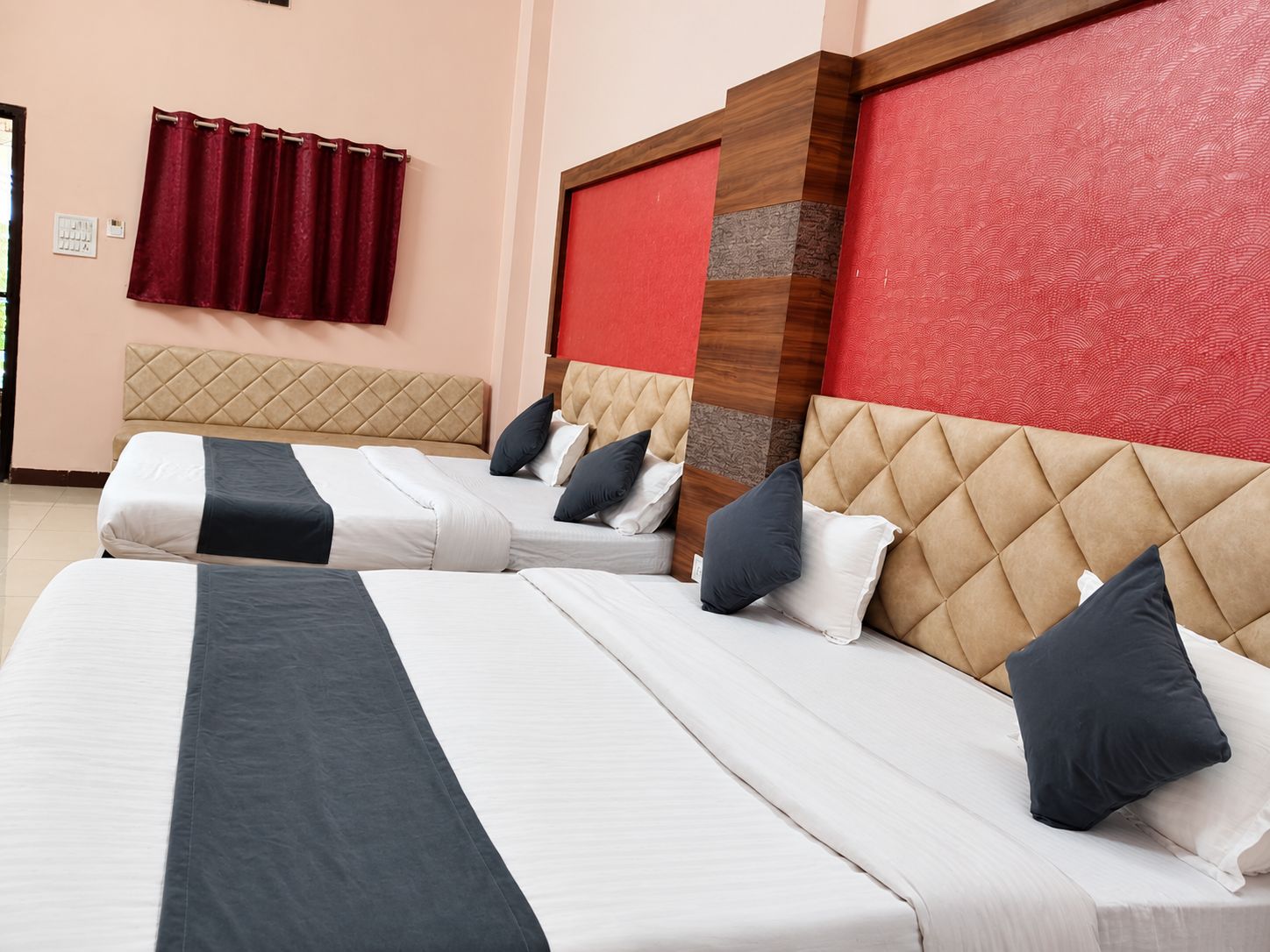 Quarto de hotel com duas camas, cada uma com cabeceira, e cortina vermelha na janela.