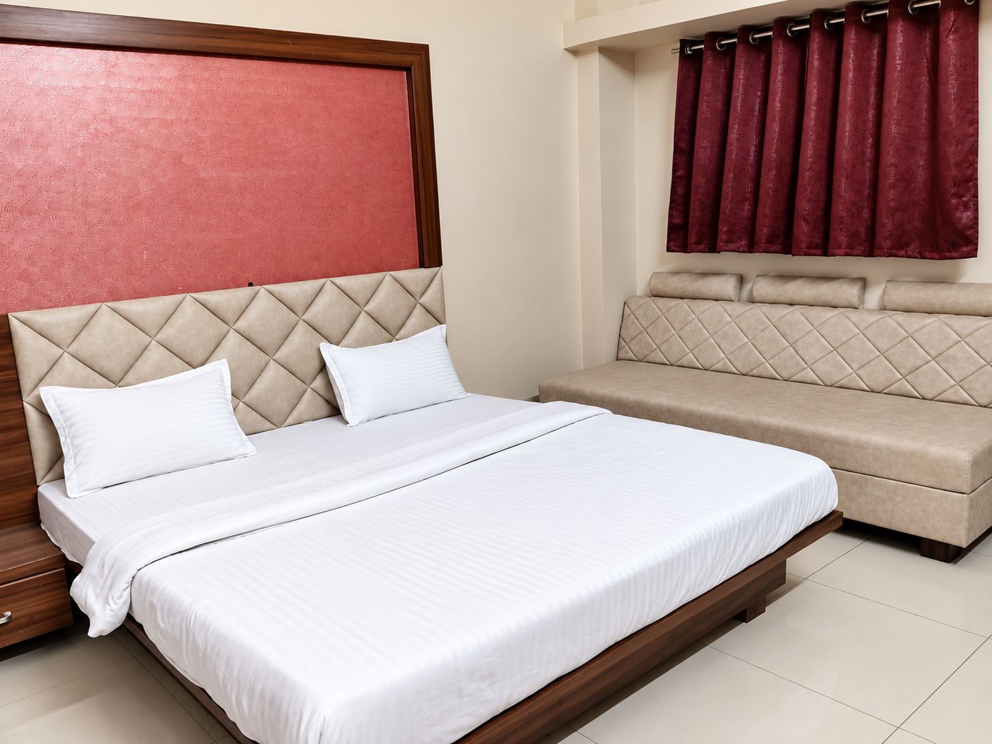 Quarto com cama, sofá, mesa de cabeceira de madeira e cortina vermelha.