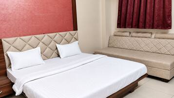 Quarto com cama, sofá, mesa de cabeceira de madeira e cortina vermelha.