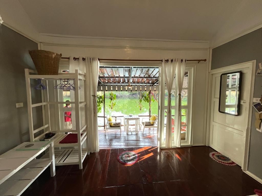 Quarto com piso de madeira, um banco branco, cesta em prateleira, vista para um pátio externo com mesa e cadeiras.