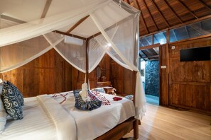Quarto com cama de dossel, paredes de madeira e vista para uma parede de pedra, além de uma televisão.