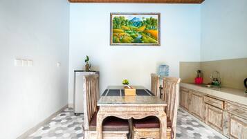 Uma área de refeições com mesa e cadeiras de madeira, um quadro na parede e uma cozinha com armários e pia.