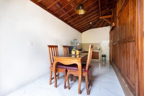 Uma sala de jantar com mesa e cadeiras de madeira, um bebedouro e uma cozinha ao fundo.