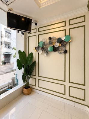 Quarto com televisão de tela plana na parede, obra de arte decorativa, uma grande planta em vaso e janela com vista para a rua.