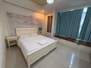Quarto com cama, mesa de cabeceira, abajur e janela com cortinas.