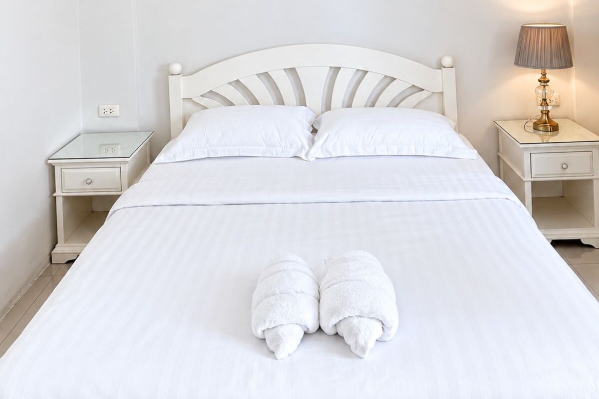 Quarto de hotel com cama, duas mesas de cabeceira, abajur e iluminação embutida no teto.