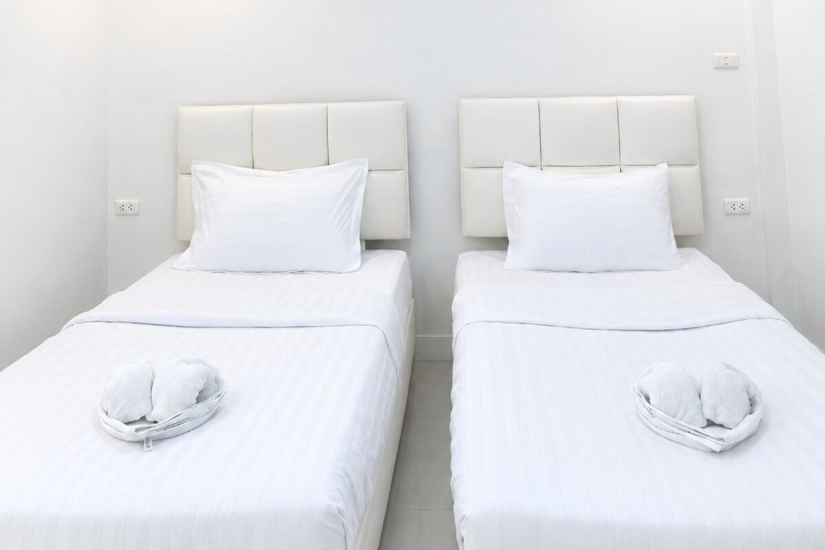 Quarto de hotel com duas camas, luminária no teto e tomada na parede.
