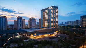 Um hotel moderno com um sinal AMORE em destaque, rodeado por edifícios altos e uma área de estacionamento bem iluminada.