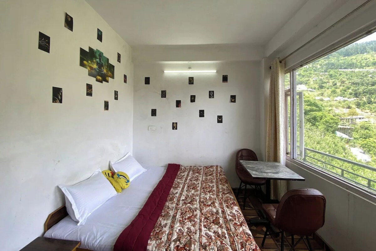 Quarto com cama, escrivaninha e vista para uma paisagem verde.