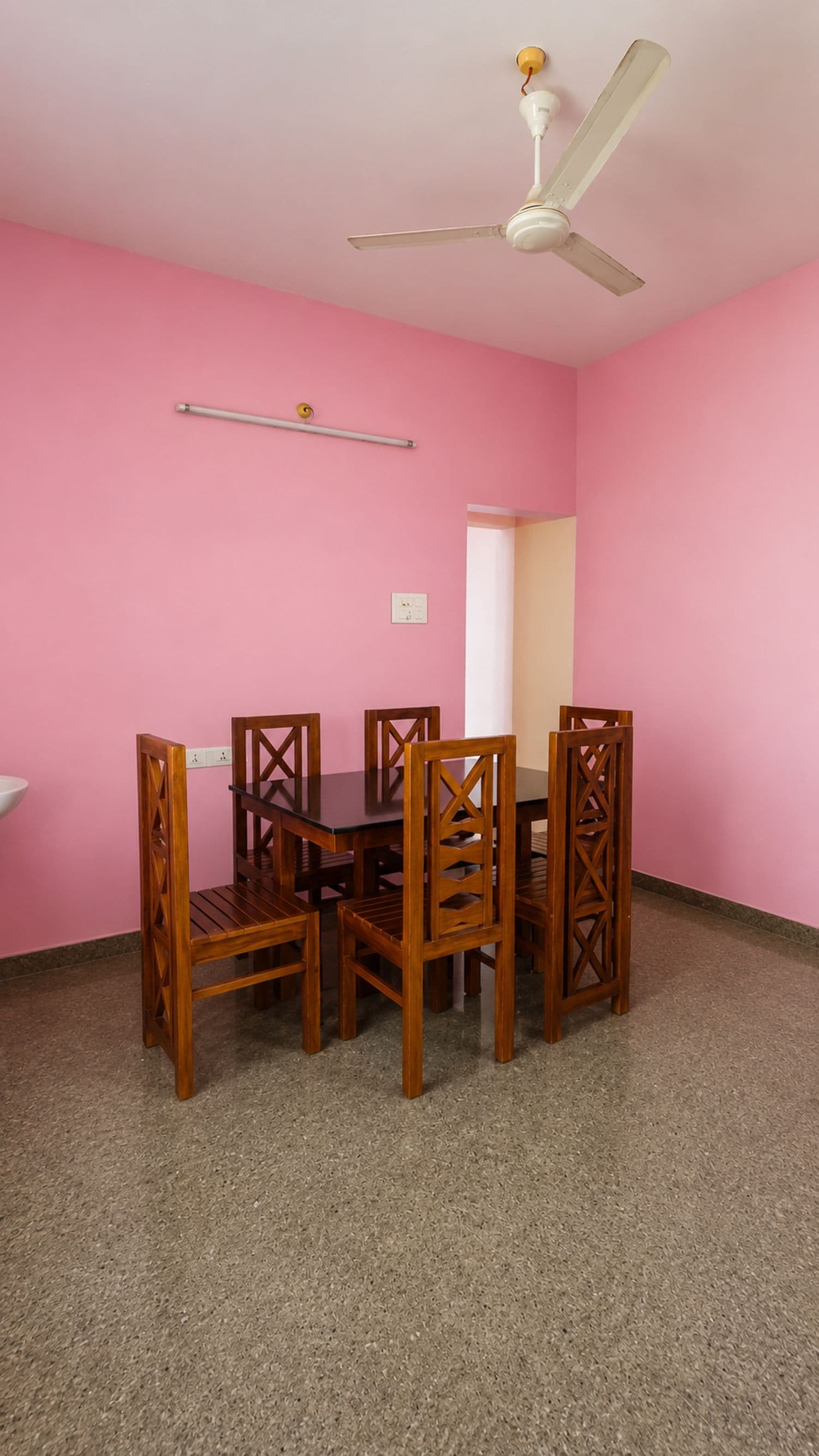 Quarto com paredes cor de rosa, ventoinha no teto, mesa com cadeiras e janela.