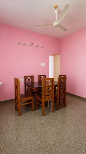Quarto com paredes cor de rosa, ventoinha no teto, mesa com cadeiras e janela.