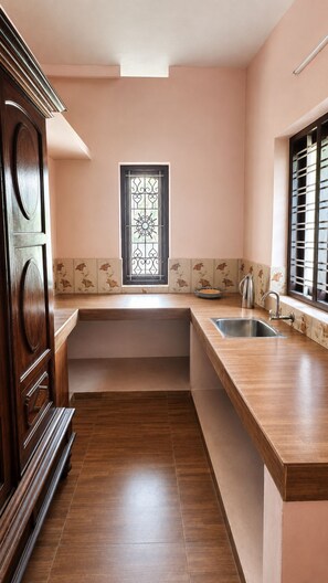 Cozinha com bancada de madeira, pia de aço inoxidável e janela decorativa.