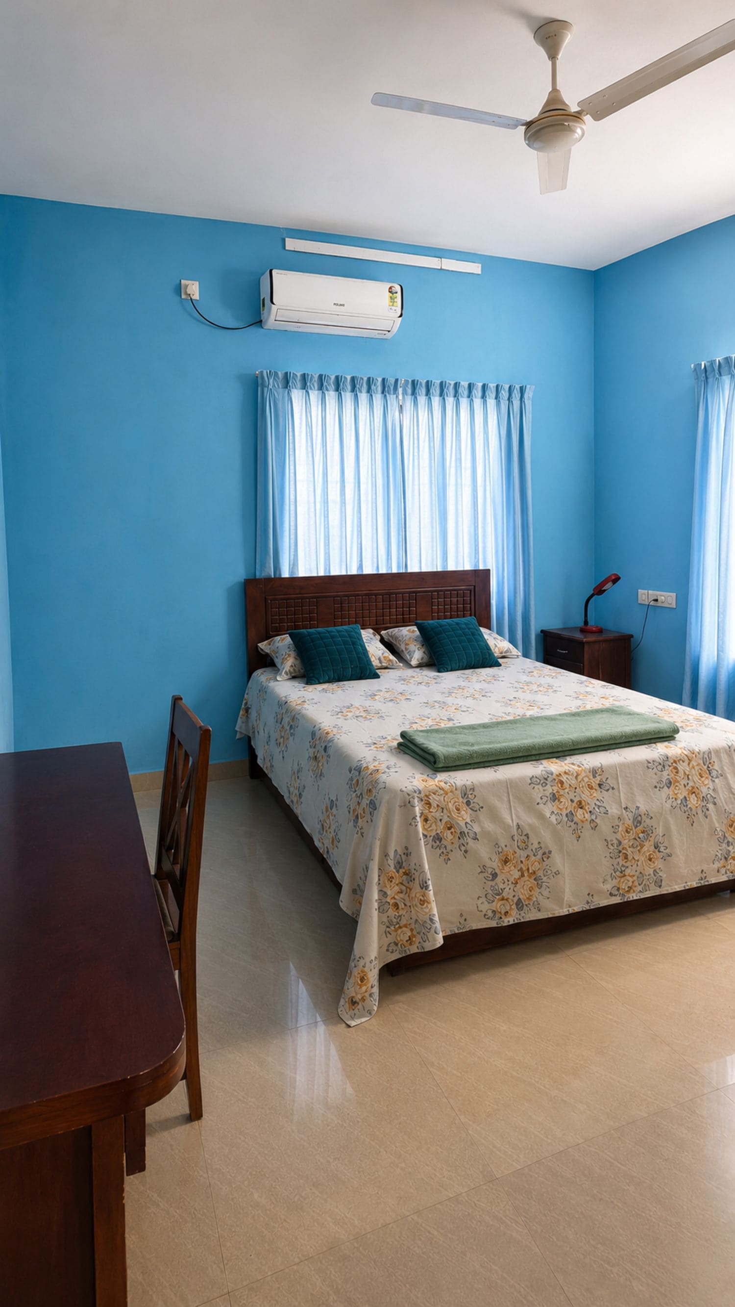 Quarto com cama, escrivaninha, cadeira, ventilador de teto e ar condicionado.