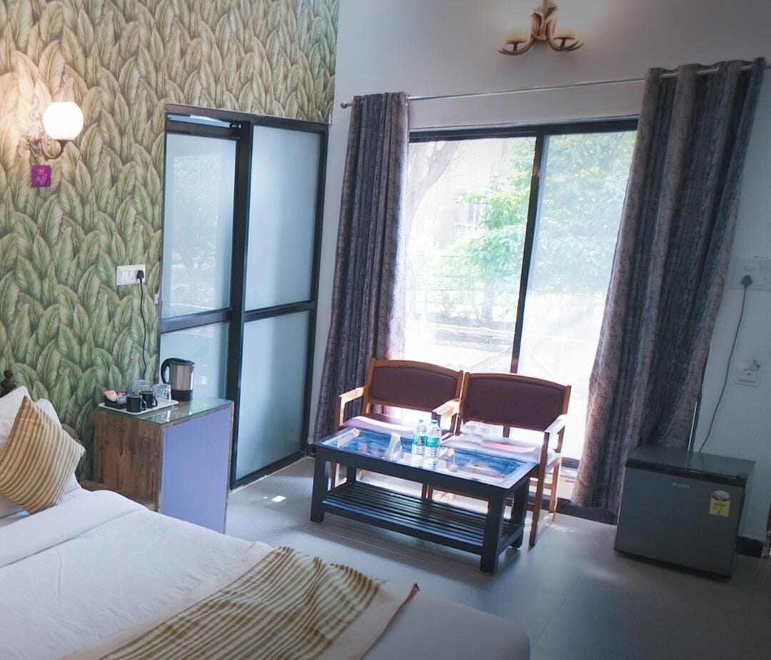 Quarto de hotel com cama, uma mesinha com cadeiras, escrivaninha e janela com cortinas.