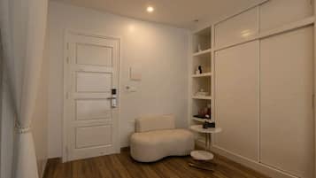 Quarto com porta branca, sofá branco, mesa redonda pequena e estantes embutidas.