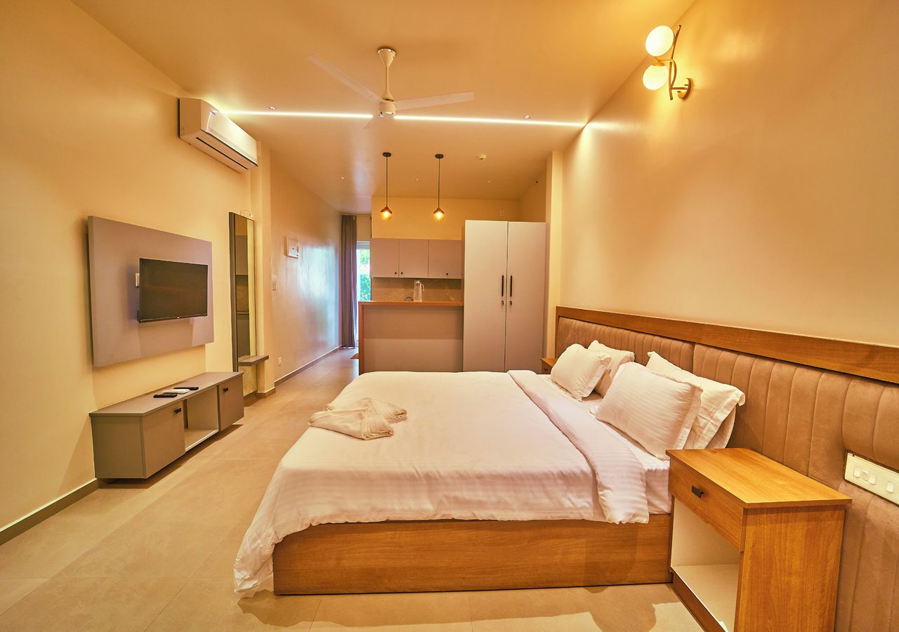 Quarto de hotel com cama, mesa de cabeceira e televisão fixada na parede.